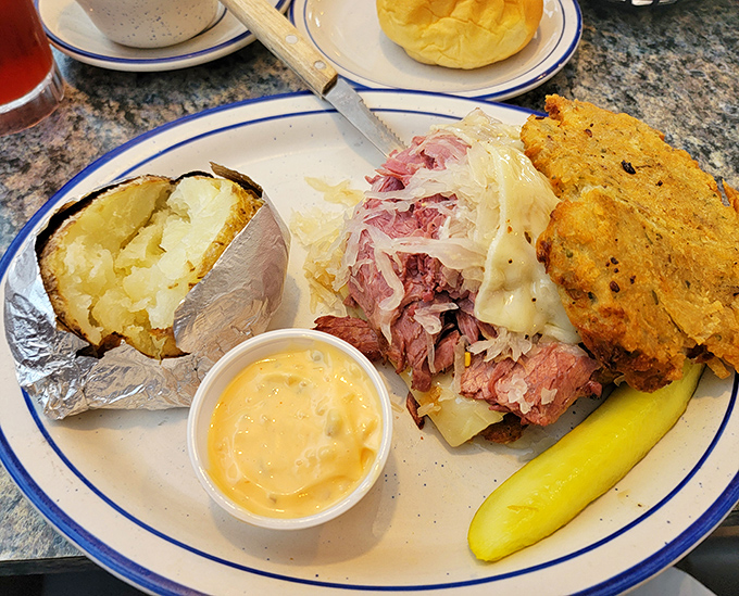 A Reuben sandwich that doesn't mess around, accompanied by a baked potato wrapped like a precious gift. Pickle included for good measure.