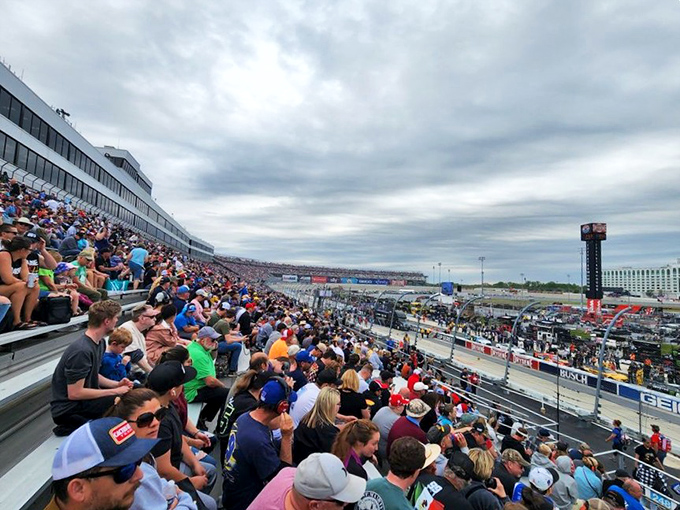 Racing enthusiasts gather beneath stormy skies, united by their appreciation for speed and seemingly unfazed by a looming monster.