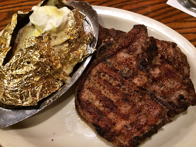 This isn't just a pork chop – it's a statement piece with perfect grill marks, paired with a loaded baked potato that's practically a meal itself.