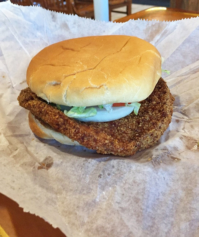 Indiana's iconic pork tenderloin sandwich in its natural habitat&mdash;crispy, golden, and hanging rebelliously over the edges of both bun and paper.