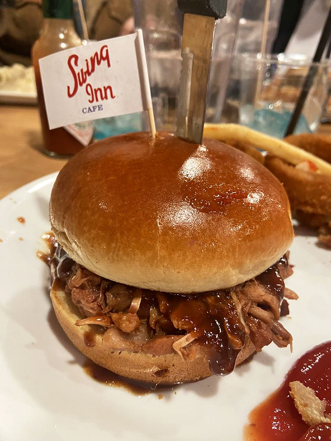 Behold the pulled pork sandwich in all its glory &ndash; tender strands of smoky meat glistening with sauce, proudly flying the Swing Inn flag like a delicious victory banner.