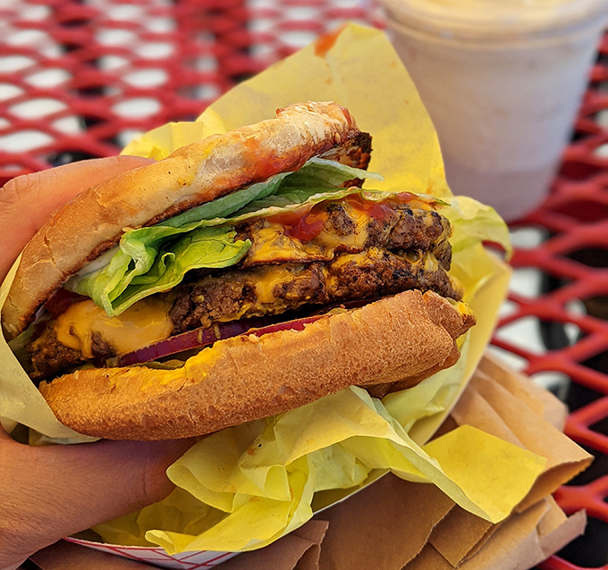 Behold the double cheeseburger in its natural habitat: wrapped in yellow paper, nestled on a red picnic table, waiting to change your day.