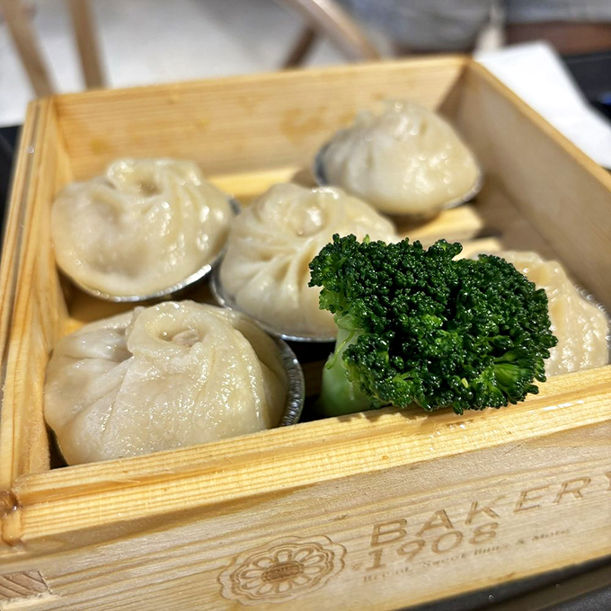 Soup dumplings sitting pretty in their wooden steamer basket&mdash;each one a self-contained flavor explosion waiting to happen. That broccoli garnish is living its best life.