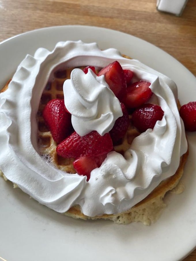 Fresh strawberries crown this waffle like nature's own edible confetti celebrating morning's arrival perfectly.