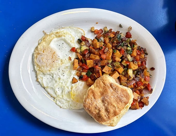 Breakfast perfection: sunny-side up eggs alongside colorful sweet potato hash that's like confetti for your taste buds, with a biscuit standing by for gravy duty.