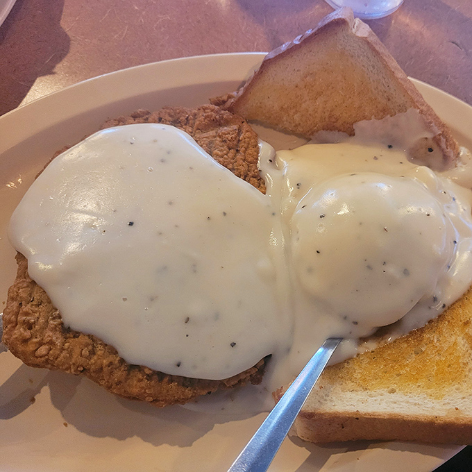 Country-fried perfection smothered in pepper-speckled gravy that could make cardboard taste good. The toast is just there to soak up the evidence.