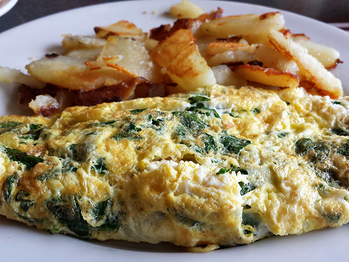 The humble omelet, elevated to art form. Fluffy eggs embrace fresh spinach while those home fries stand by, ready for their supporting role.