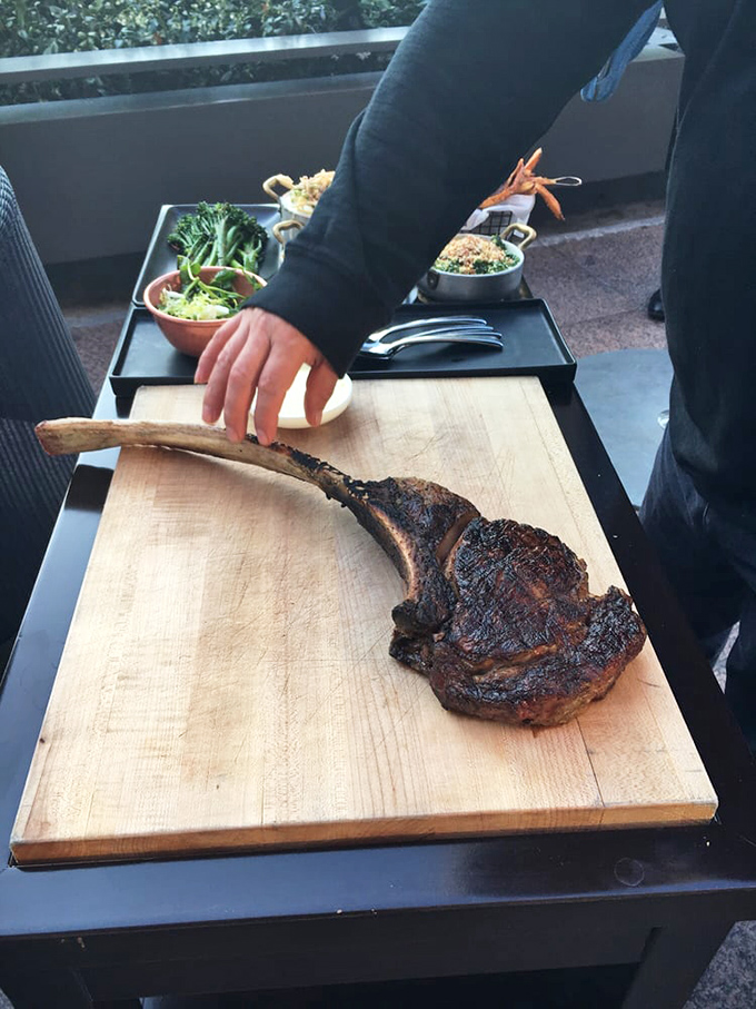 The tomahawk steak makes its dramatic entrance—part prehistoric weapon, part culinary masterpiece. Side dishes playing supporting roles in this meaty blockbuster.