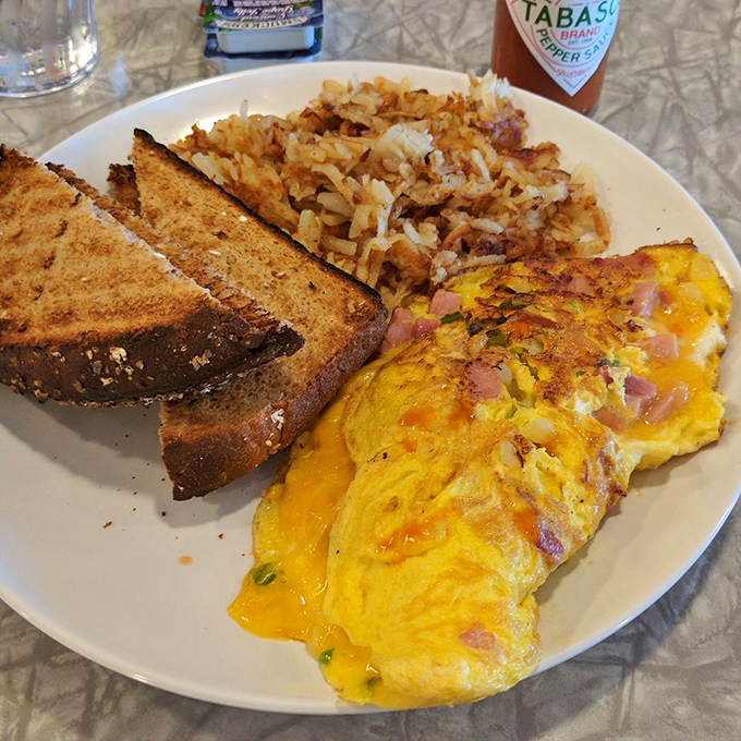 The holy trinity of breakfast: a perfectly executed omelet, crispy hash browns, and toast ready for butter application. Morning glory on a plate.