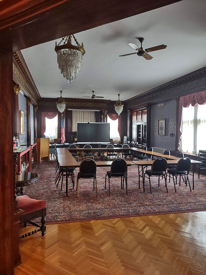 Once a room for entertaining society's elite, now school administrators debate budgets beneath chandeliers that have witnessed both gilded splendor and fluorescent practicality.