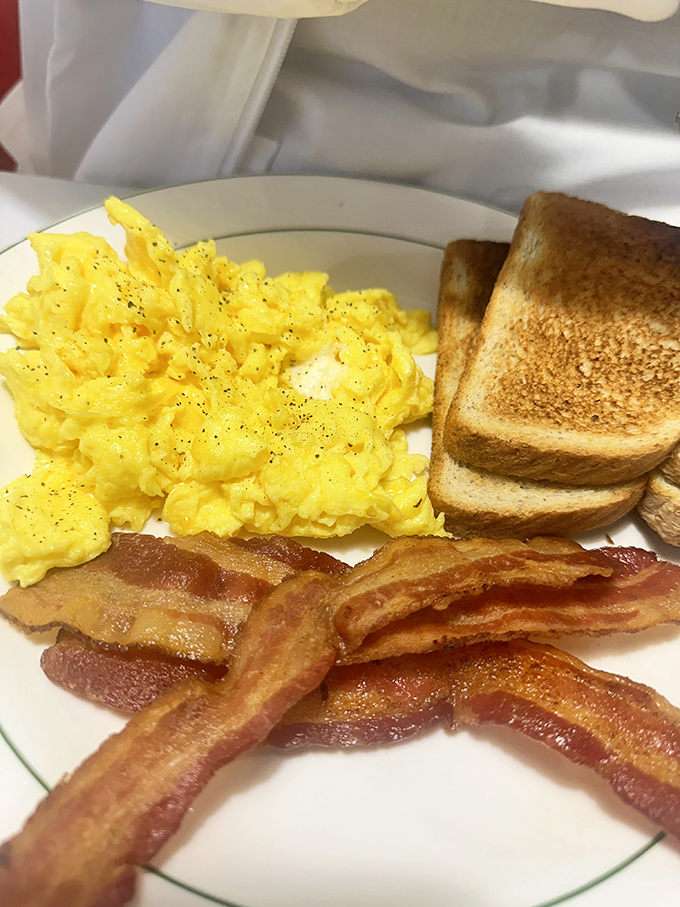 The holy trinity of breakfast perfection: fluffy scrambled eggs, perfectly crisped bacon, and toast waiting patiently for its butter bath.