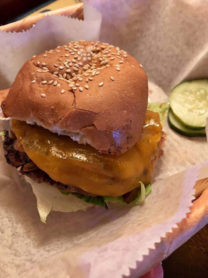 A sesame-studded bun crowns this masterpiece like a royal hat, with cheese melting down the sides like delicious golden waterfalls