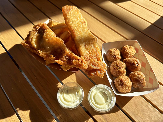 Fish and chips with a side of hush puppies&mdash;the holy trinity of fried goodness. Sunlight makes everything look like it was blessed by the fryer gods.