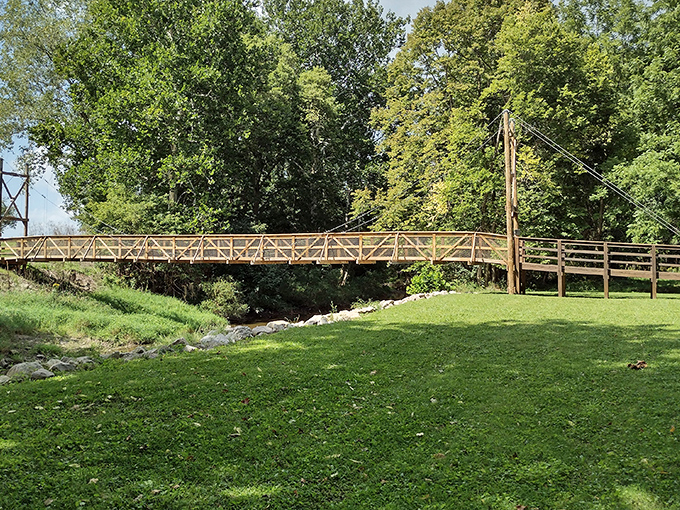 This rustic footbridge seems to whisper, "Cross me if you dare," connecting two verdant shores over a gentle stream in perfect small-town tranquility.