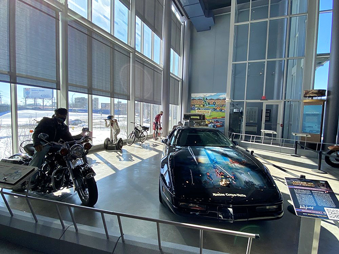 Modern meets vintage in this striking display featuring a sleek black sports car alongside classic motorcycles, showcasing America's diverse transportation evolution under natural light.