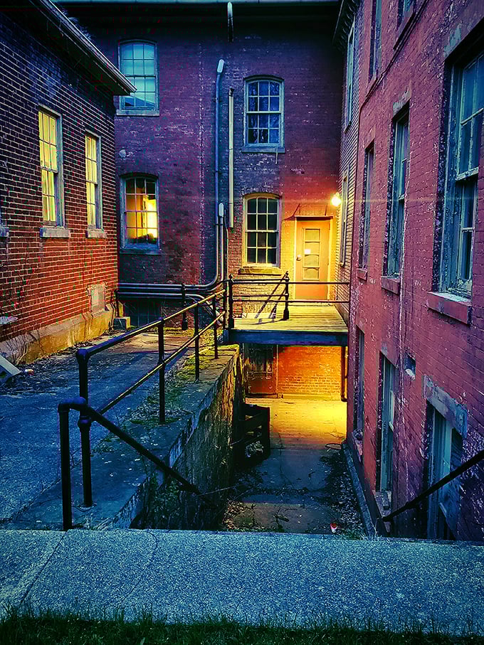 Twilight transforms the building's courtyard into a scene from a gothic thriller, the warm glow of a single light beckoning like a false promise.