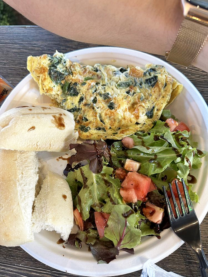 The legendary spinach omelet arrives like a golden sunrise, perfectly folded and accompanied by a fresh garden salad.