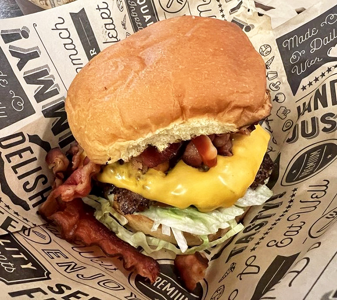 The bacon cheeseburger arrives like a beautiful, messy promise. That crispy bacon strip is practically waving hello, daring you to take the first bite.