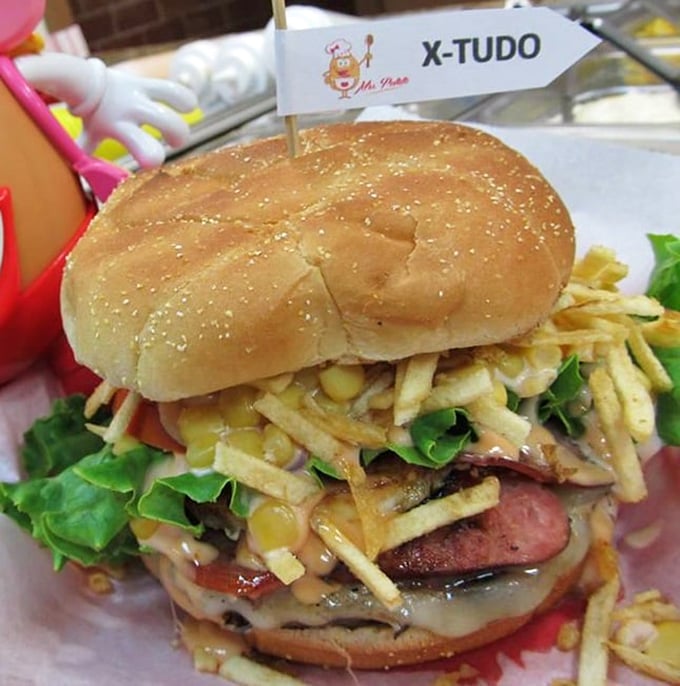 The X-Tudo burger defies gravity and conventional burger wisdom&mdash;stacked with potato sticks, ham, corn, and enough toppings to require a strategic eating plan.