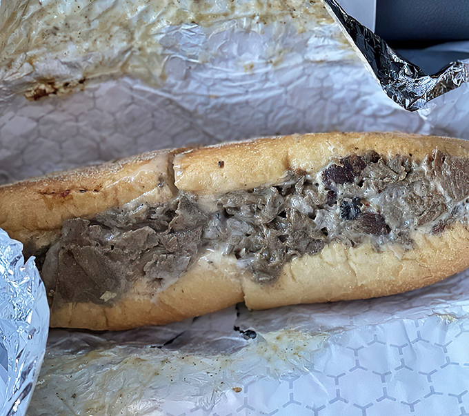 The cheesesteak in its natural habitat&mdash;wrapped for travel but barely containing its savory treasures within that pillowy roll's embrace.