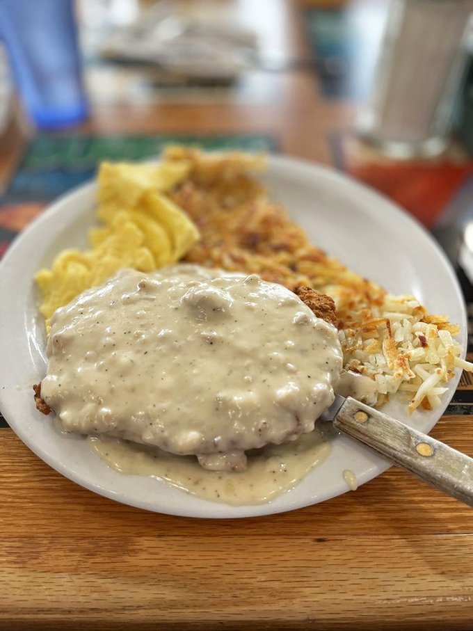 Country gravy cascades over crispy chicken fried steak like a delicious avalanche, with hash browns and eggs playing perfect supporting roles.
