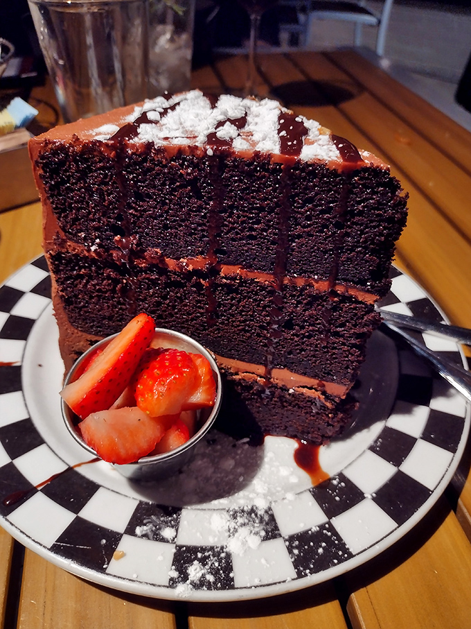 A slice of chocolate cake so tall and imposing it deserves its own zip code. The side of berries is just pretending this is somehow balanced.
