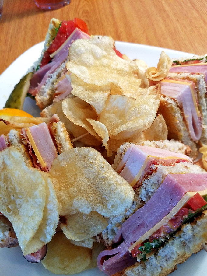 A club sandwich that's architectural brilliance&mdash;layers of ham, turkey, and fresh vegetables between homemade bread, with chips standing guard like crispy sentinels.