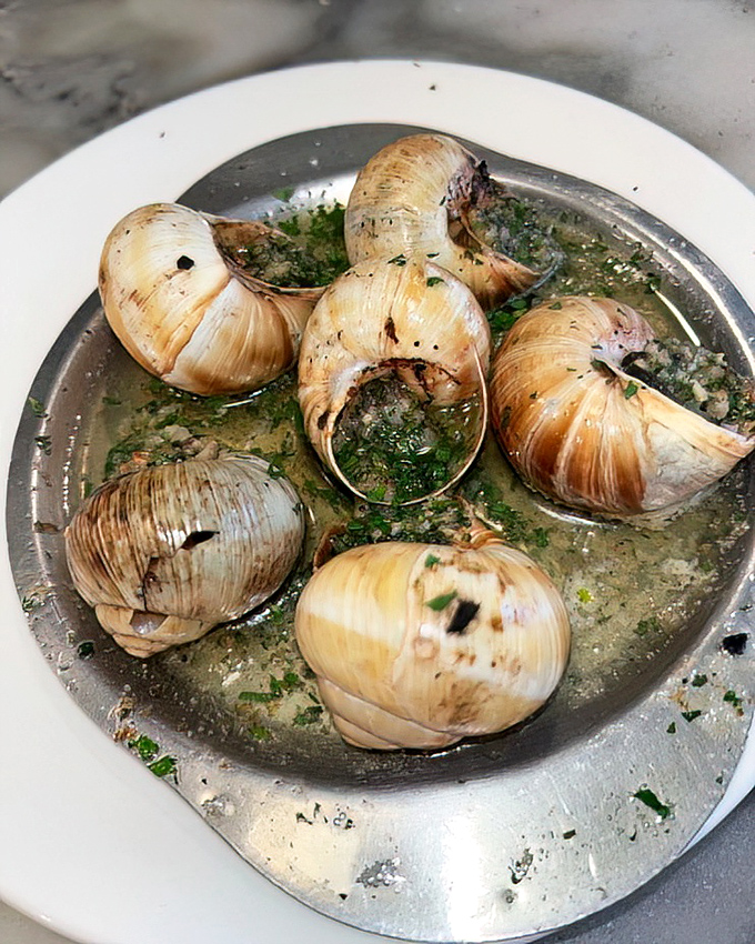 Escargot: where garlic butter transforms garden visitors into gourmet delicacies. These little flavor bombs make you wonder why you ever feared eating snails.