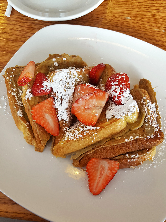 French toast that's achieved celebrity status, adorned with fresh strawberries and powdered sugar like it's walking the breakfast red carpet.