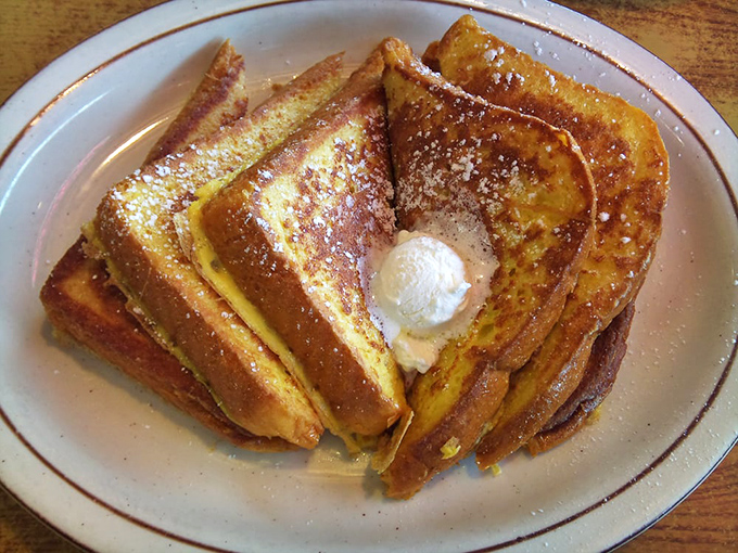 French toast stacked like golden pillows, dusted with powdered sugar, and crowned with a butter pat that's melting into breakfast nirvana.