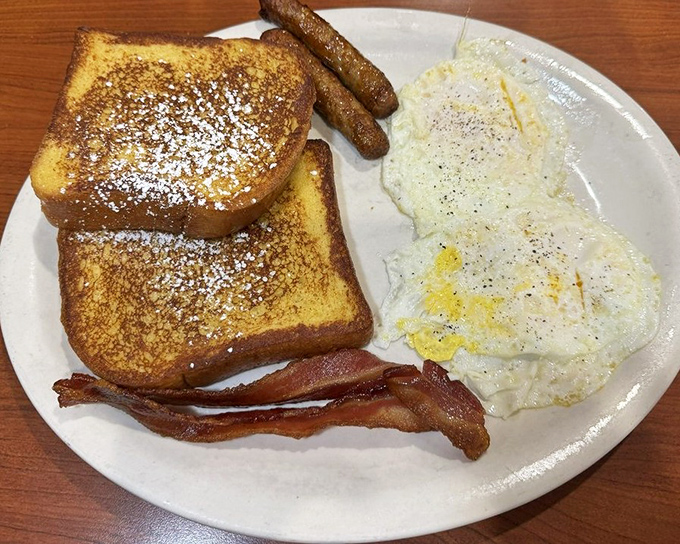 French toast that's dressed for success with a dusting of powdered sugar, flanked by the breakfast trinity of eggs, bacon, and sausage.