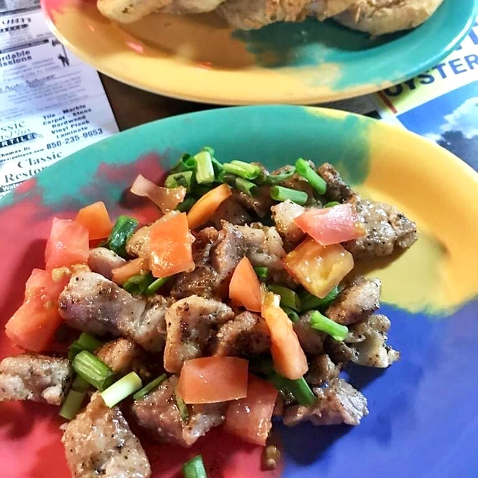 This colorful plate showcases what appears to be seasoned fish or seafood topped with fresh tomatoes and green onions&mdash;simple ingredients elevated by expert preparation.