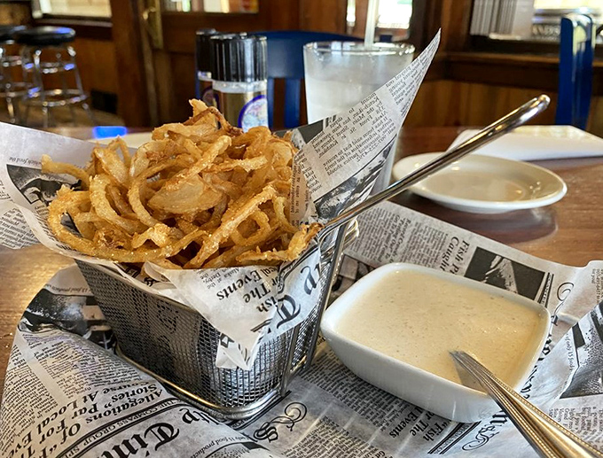 Haystack Onions that crunch loud enough to turn heads, served newspaper-style with a dipping sauce worth bottling and taking home.
