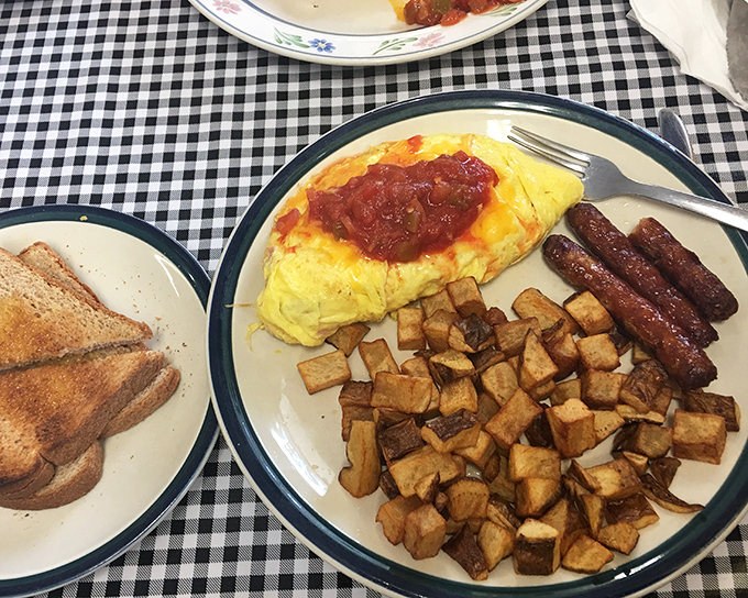 The breakfast trinity: perfectly folded omelet, crispy home fries, and sausage links. A plate that says "good morning" better than words ever could.