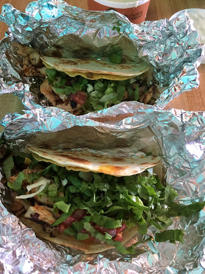 Two tacos nestled in foil like precious cargo. The fresh lettuce and perfectly grilled tortillas promise a textural adventure worth every calorie.