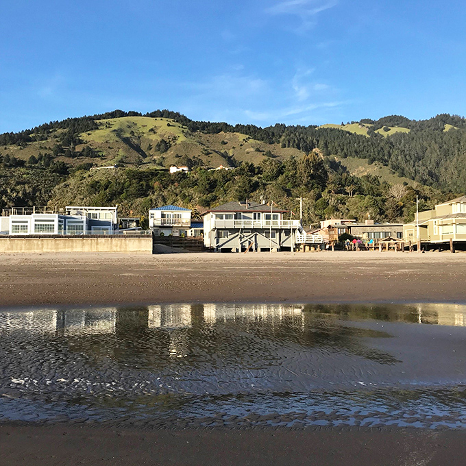 Beach homes reflect in the wet sand at low tide, creating mirror images so perfect you'd think Mother Nature was showing off her Instagram skills.