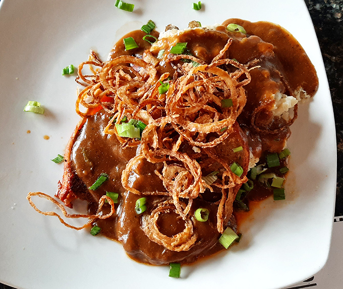 Meatloaf elevated to an art form, crowned with crispy onion strings and swimming in gravy rich enough to make a vegetarian question their life choices.