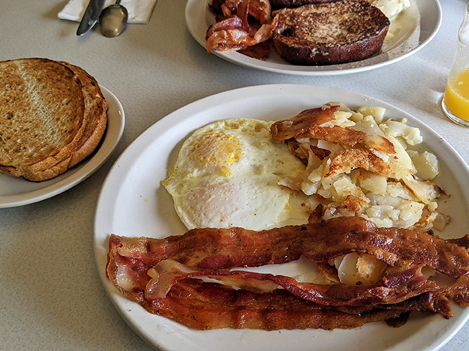 The holy trinity of breakfast: crispy bacon, eggs with those perfectly frilled edges, and home fries that actually taste like they've met a potato.