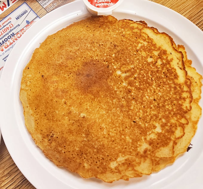 Golden-brown pancake perfection that spans the plate like a breakfast frisbee, ready for whatever toppings you dare add.