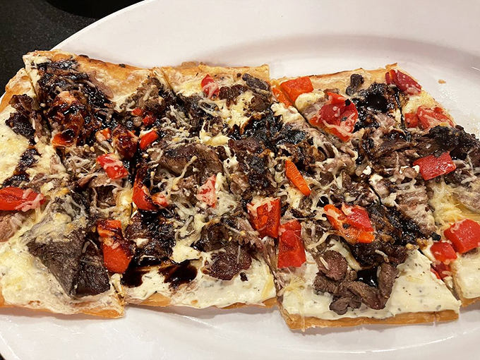 The flatbread arrives like a savory mosaic of tender beef, roasted peppers, and melted cheese&mdash;a shareable masterpiece that rarely gets shared.