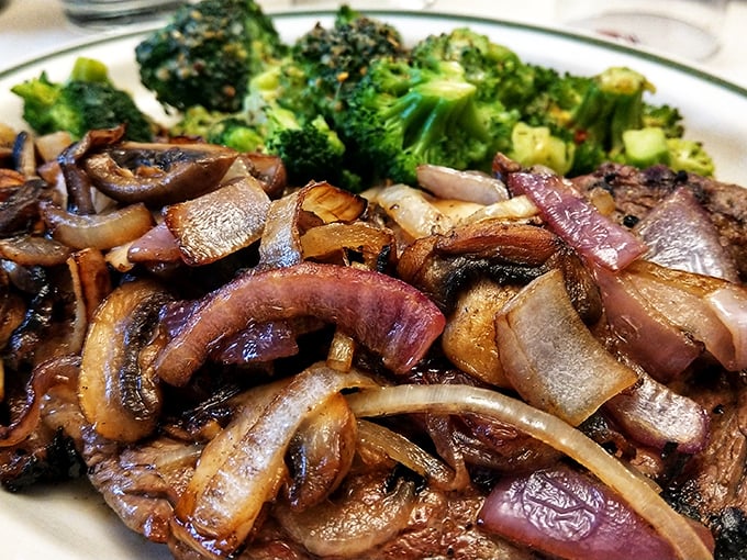 A symphony of caramelized onions crowns this perfectly seared ribeye, proving that sometimes the simplest preparations yield the most profound flavors. 