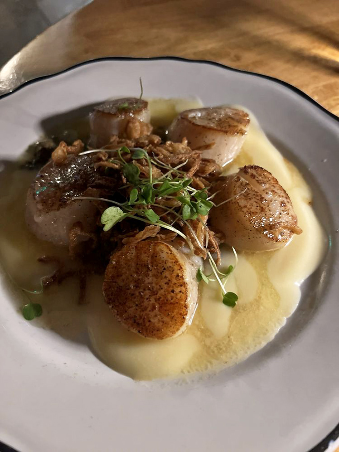 Perfectly seared scallops resting on a cloud of puree—like butter that somehow learned to swim. The microgreens add that touch of elegance.