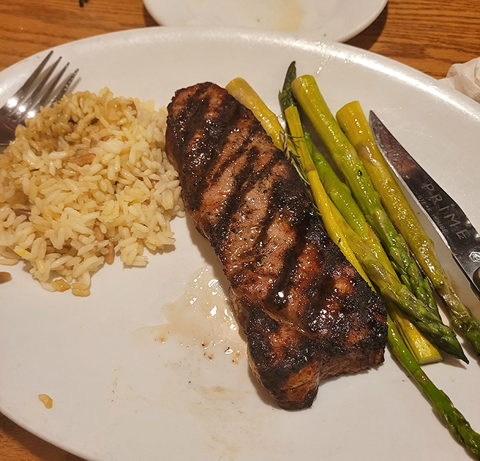 This strip steak's perfect grill marks tell a story of careful preparation, while the asparagus and rice stand by like loyal sidekicks to the beefy superhero.