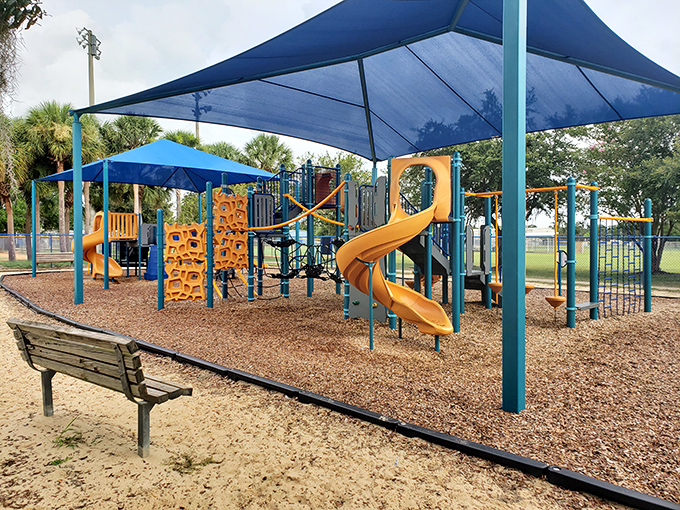 This playground offers shaded fun for grandkids while you recover from their endless energy on that strategically placed bench.
