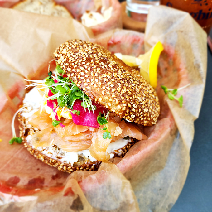 The sesame seed bialy cradles house-cured salmon, microgreens, and vibrant radish – breakfast elevated to an art form.