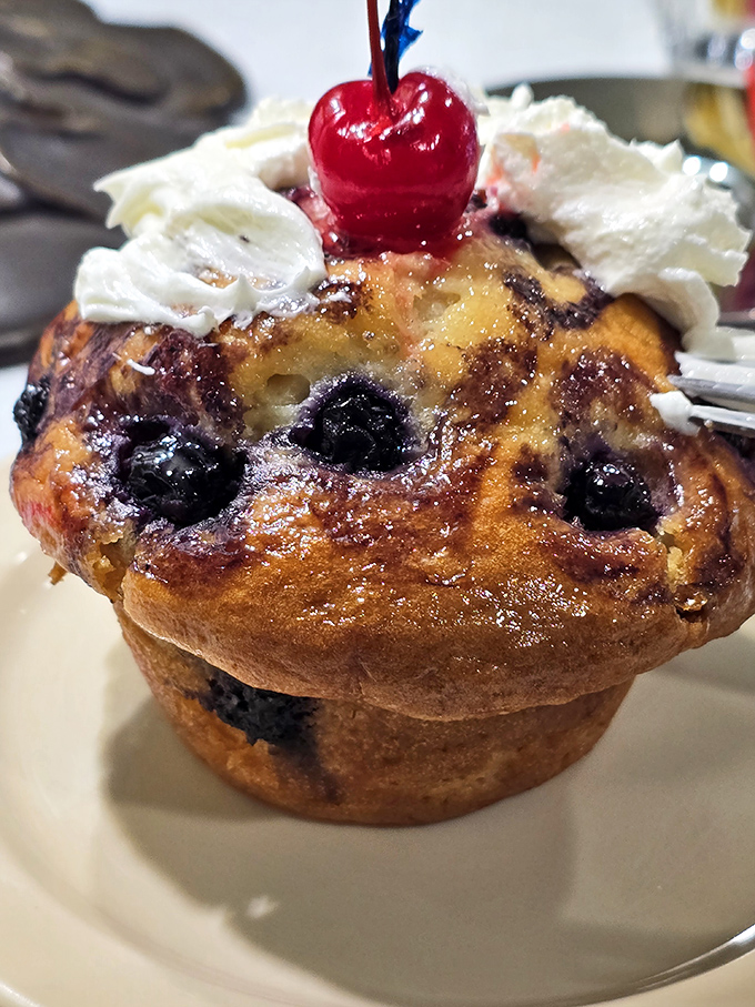 This blueberry muffin isn't just baked - it's been elevated to art form, crowned with whipped cream and a cherry like breakfast royalty.