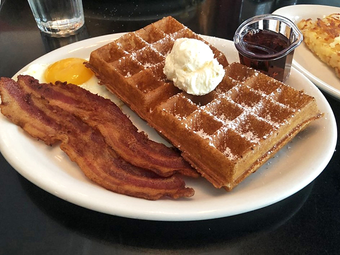 Belgian waffles dusted with powdered sugar, accompanied by bacon that could make a vegetarian question their life choices.