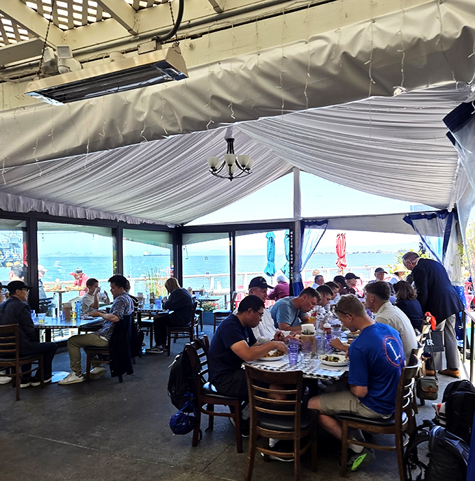 The covered dining area offers panoramic bay views that turn lunch into theater, where the water provides both backdrop and conversation starter.