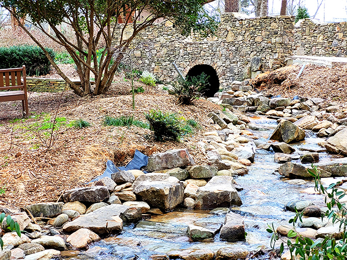 Water doesn't just flow here – it dances, creating nature's soundtrack as it tumbles over carefully arranged stones beneath the stone arch.