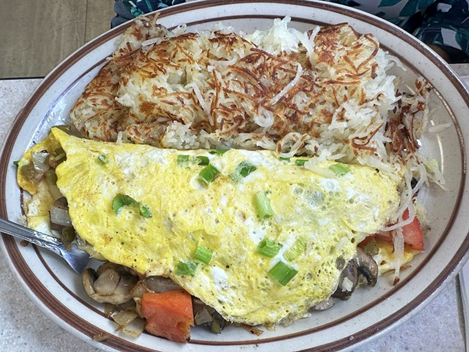 An omelet bursting with fresh vegetables, nestled beside hash browns that could double as golden roof shingles.